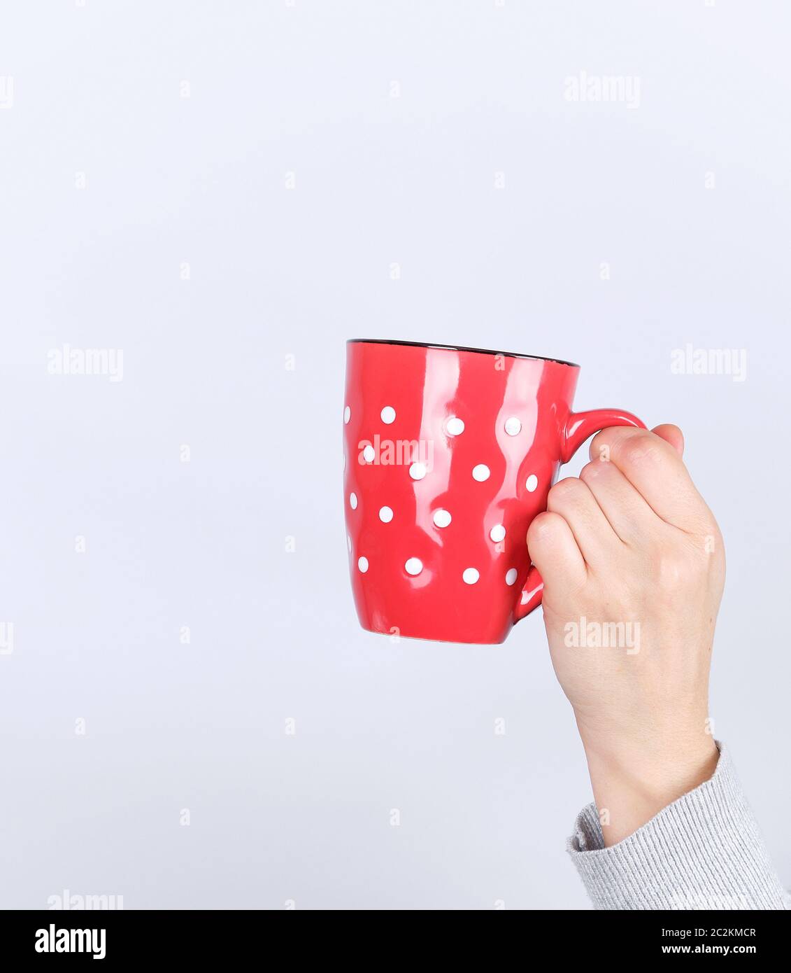 red ceramic cup in a female hand on a white background, hand is raised ...