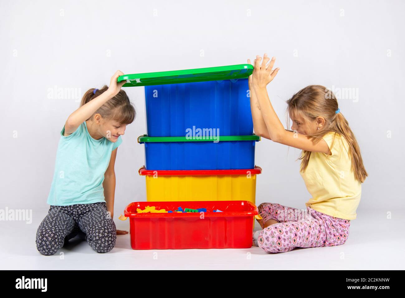 Two girls opened the lid of a large plastic box with toys, and look ...
