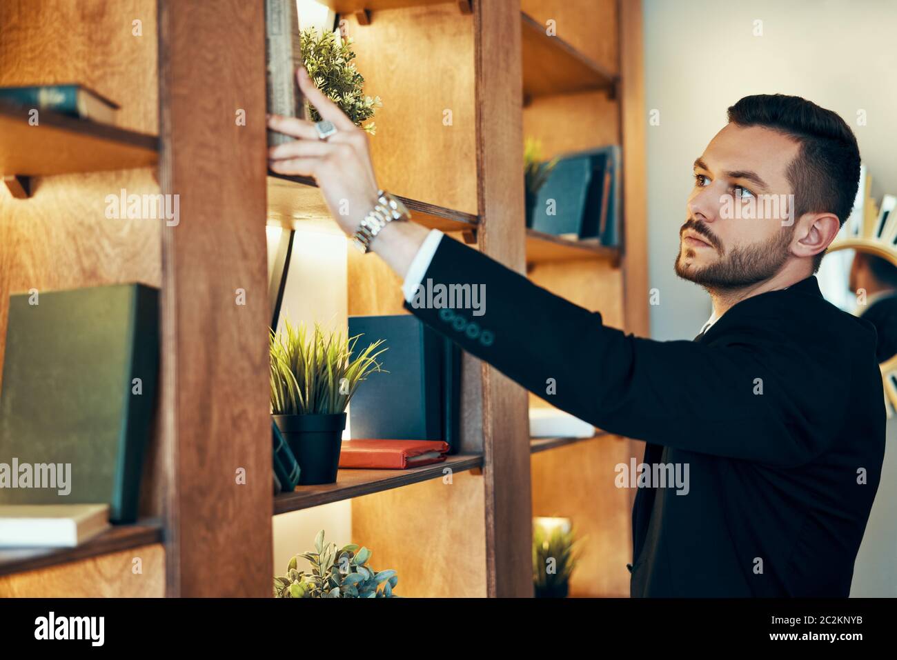 Elegant man taking book from bookshelf Stock Photo - Alamy