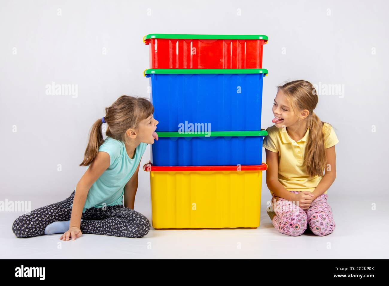 Two Girls Peek From Different Sides Of Large Plastic Boxes And Show