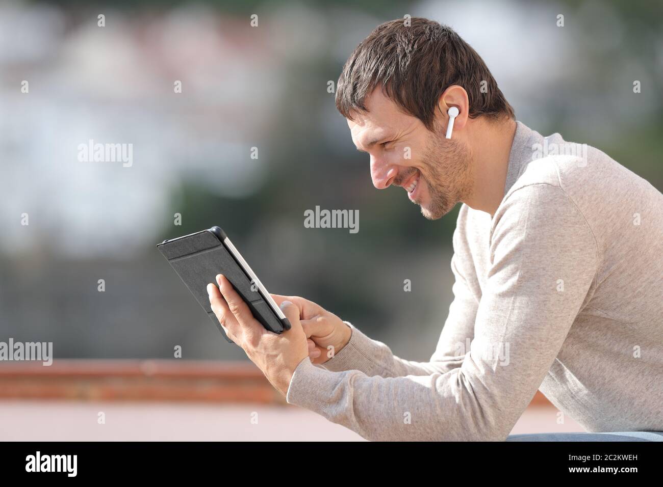 Profile of happy man watching media with tablet and wireless earbuds ...