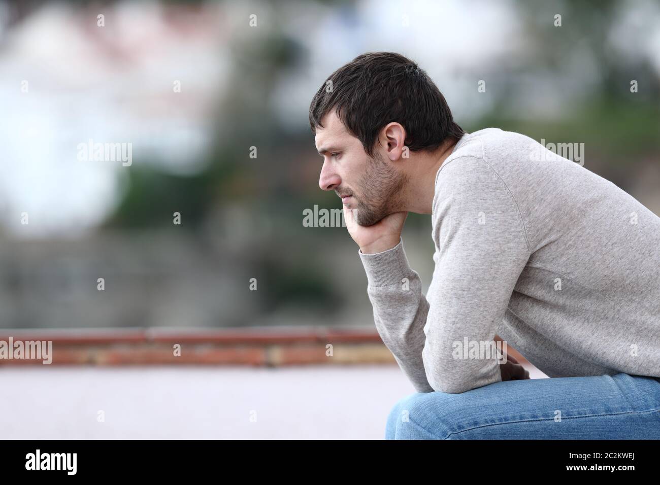 Pensive worried man sitting on a bench alone in a town Stock Photo - Alamy