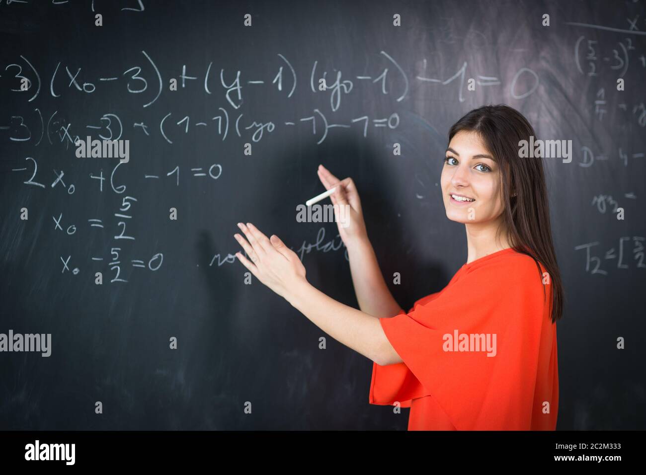 Pretty, young college student writing on the chalkboard/blackboard ...