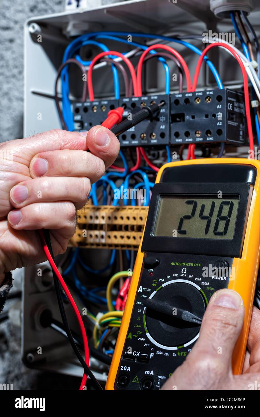 Electrician with multimeter tester measures the voltage in a ...