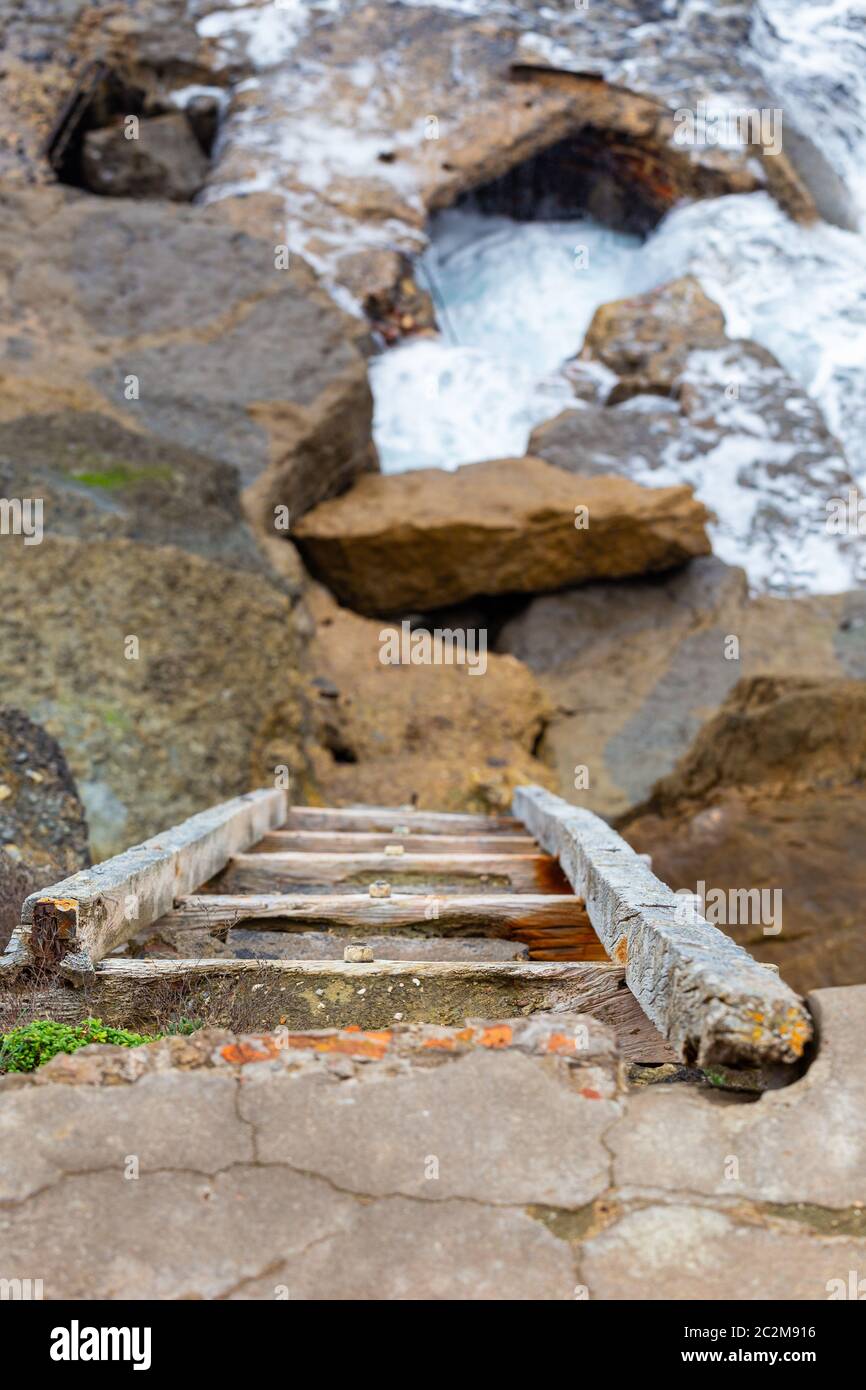 old wooden ladder on rock cliff on ocean coast. the view from the top ...