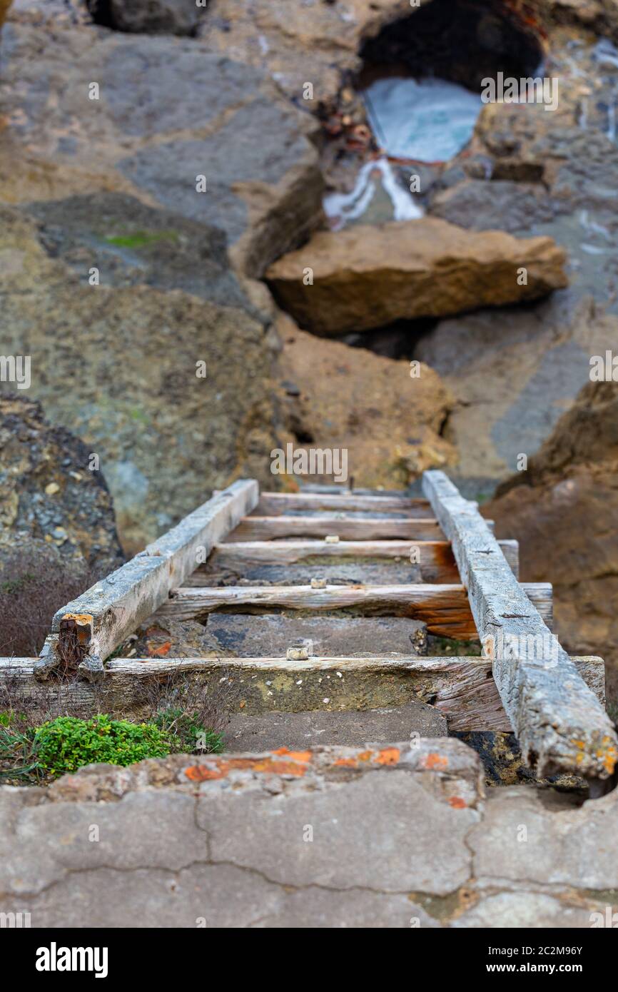 old wooden ladder on rock cliff on ocean coast. the view from the top ...