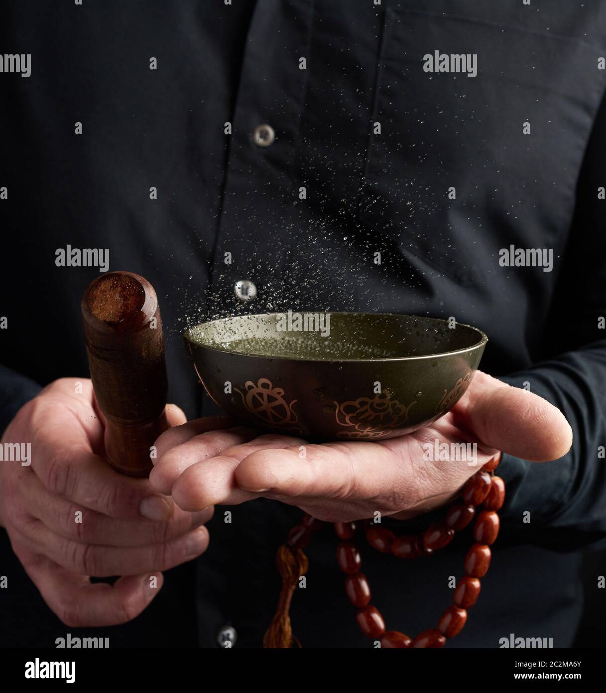 adult man in a black shirt rotates a wooden stick around a copper ...