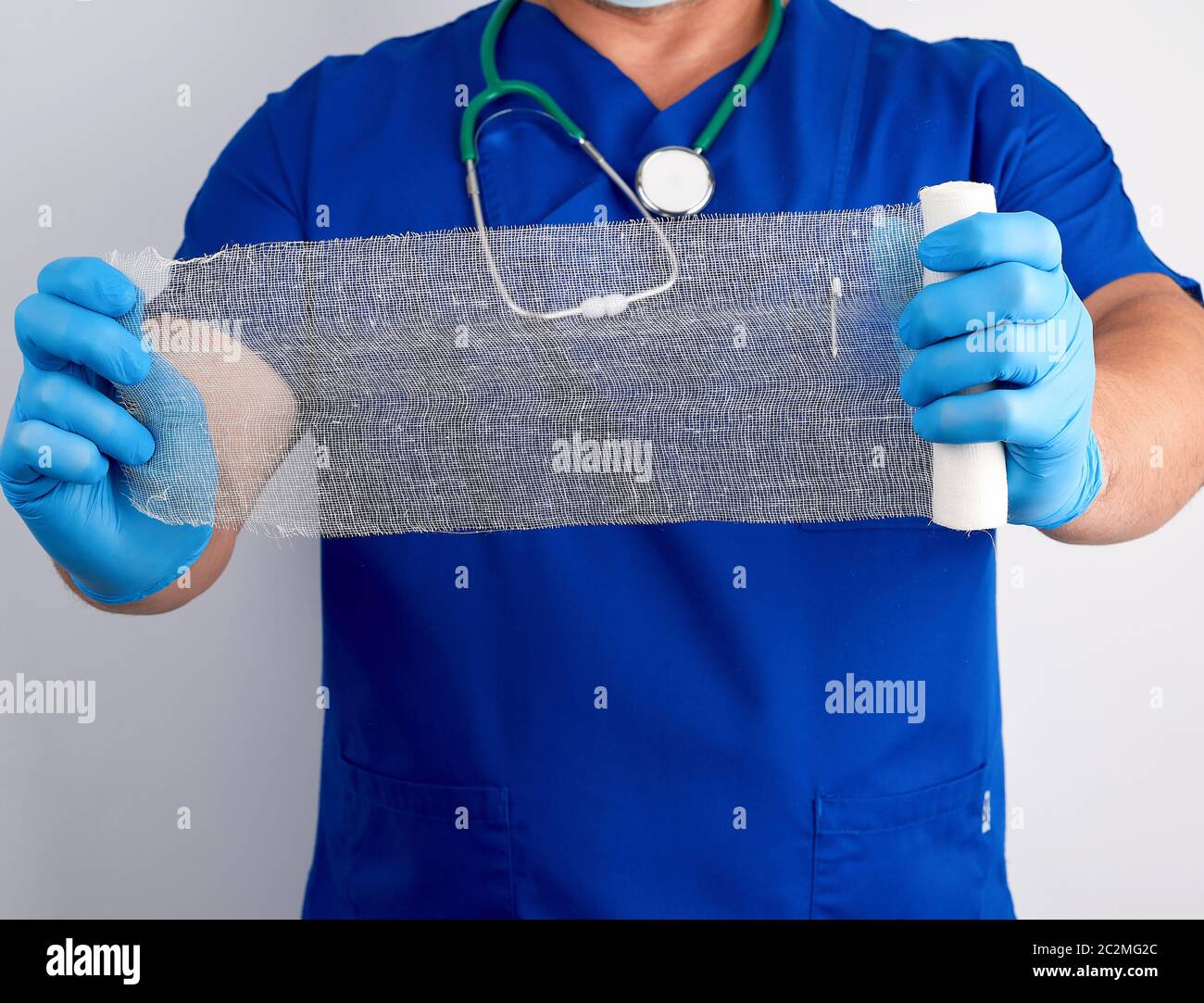 doctor in blue uniform and latex gloves holds a roll of white bandage ...
