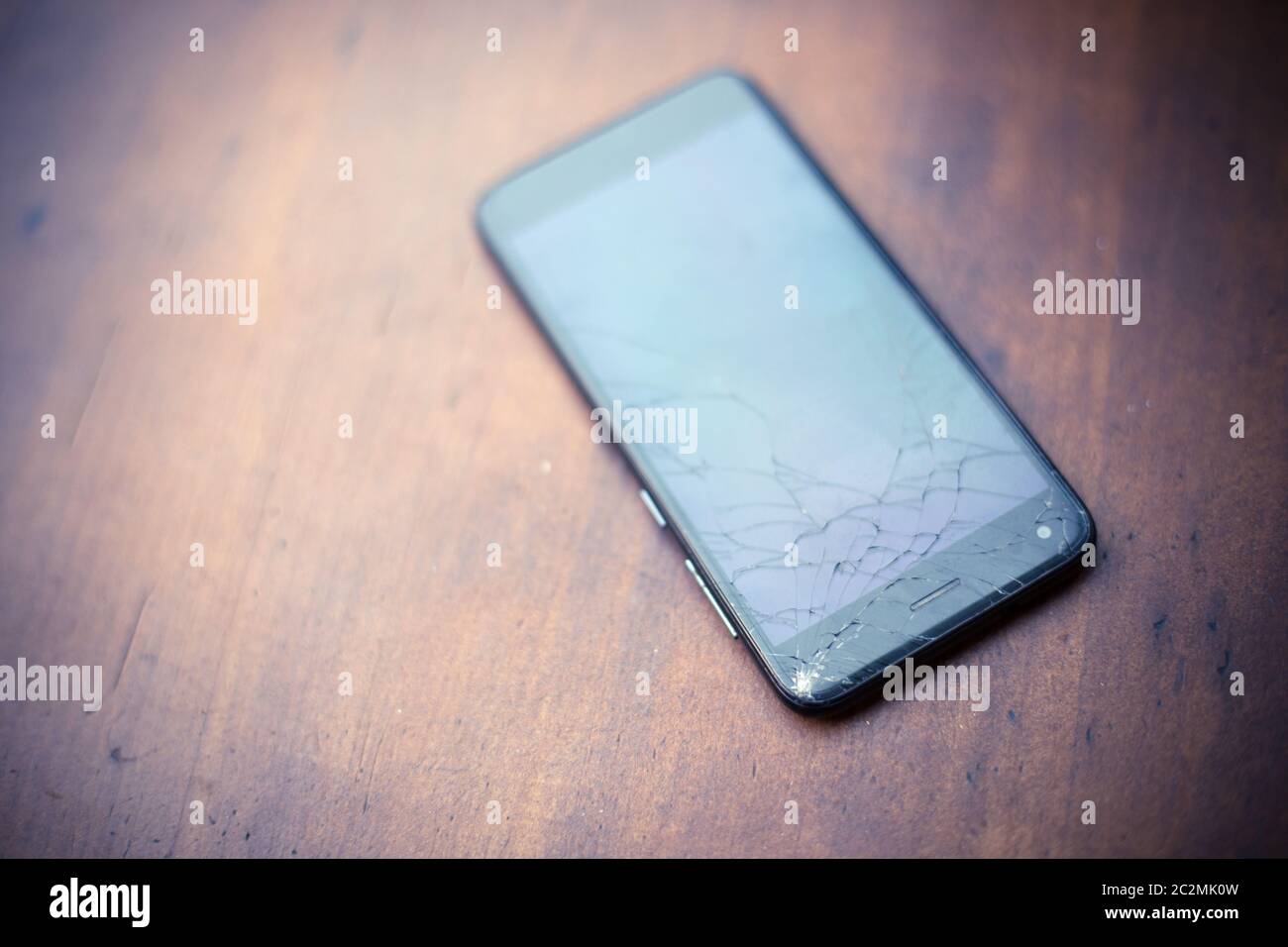 Close up shot of a mobile phone with broken screen on a wooden table ...