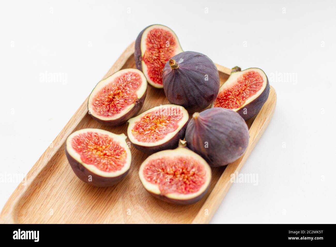 halves of fresh juicy figs in a wooden plate on a white background ...