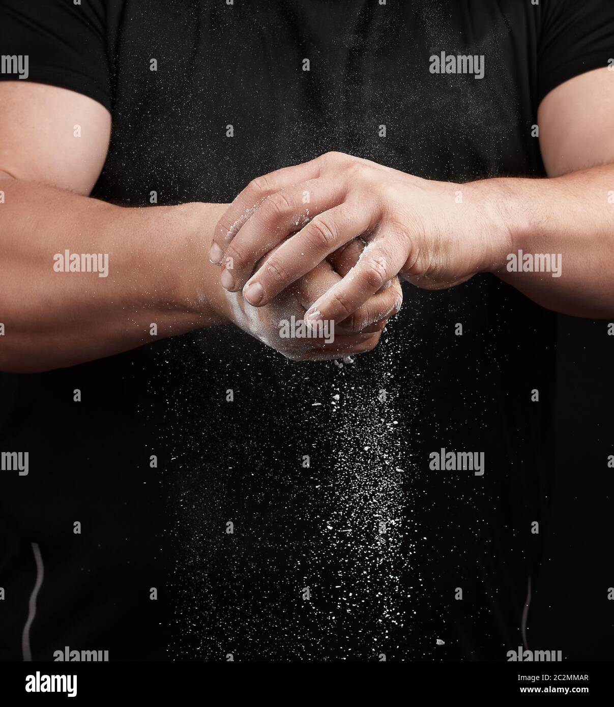 muscular athlete in a black uniform rubs his hands with white dry ...