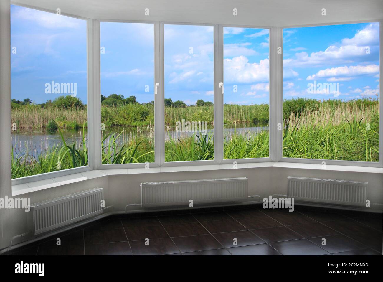 Room with wide window overlooking landscape with lake surrounded with ...