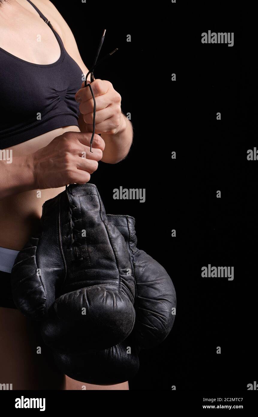 girl with muscular body holds a pair of old black boxing gloves, she is ...