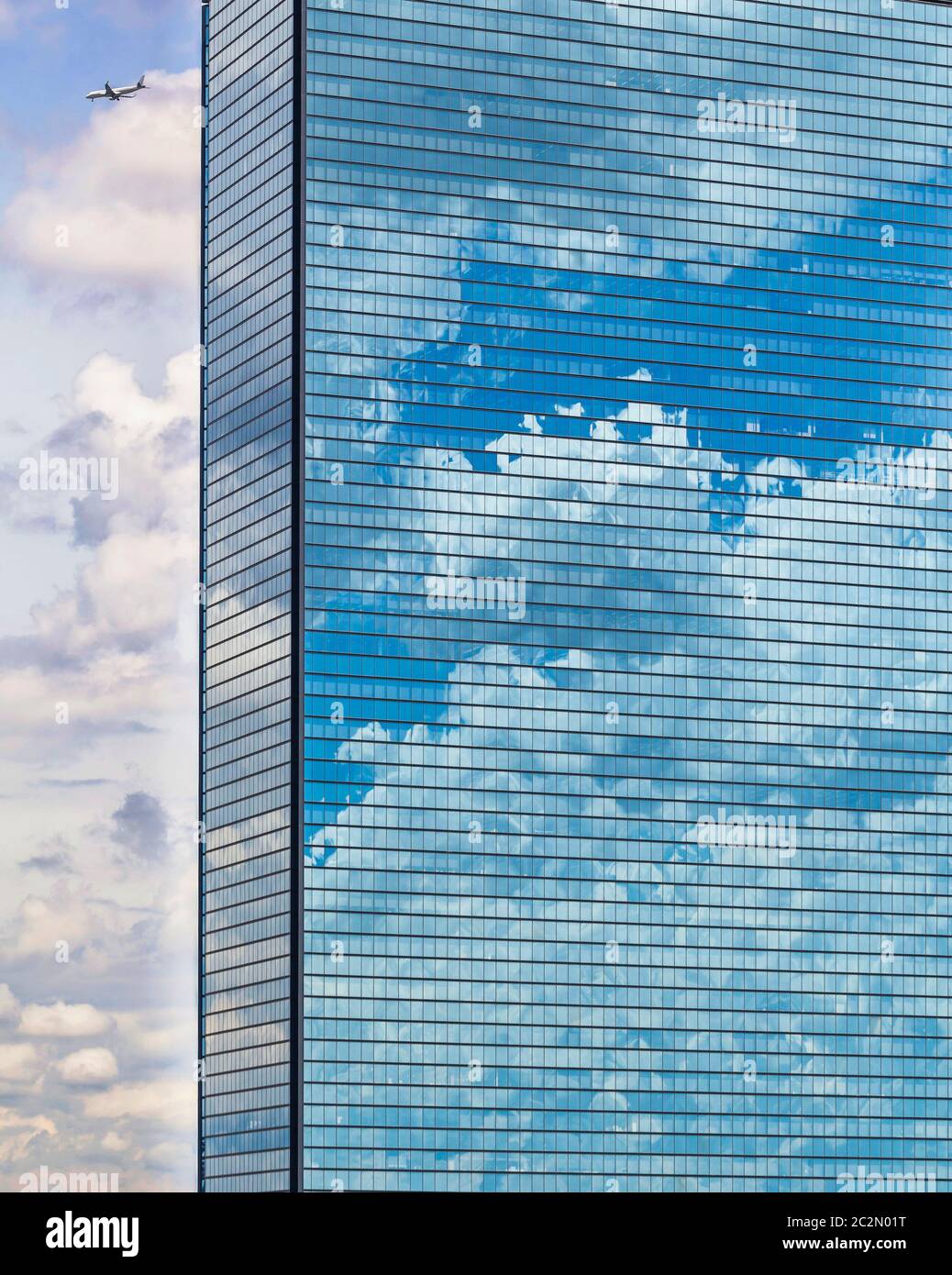 Plane flies over a skyscraper reflecting clouds in windows Stock Photo ...