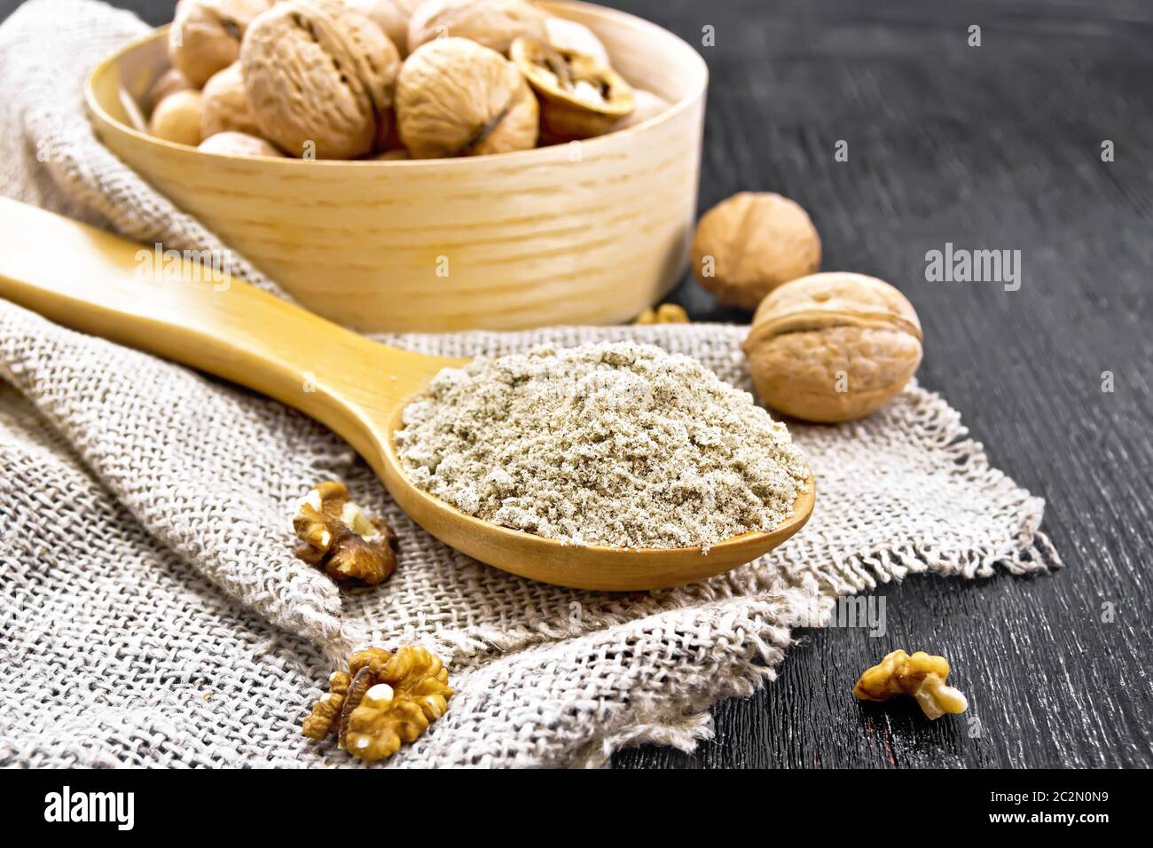 Walnut flour in a spoon on burlap, nuts on a table and in a bowl on ...