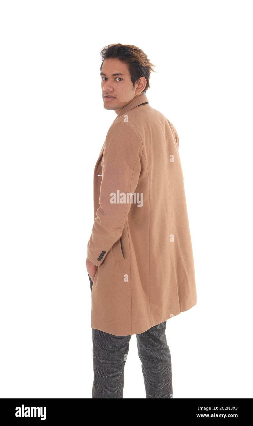 A tall young man standing in a beige coat from the back in the studio ...