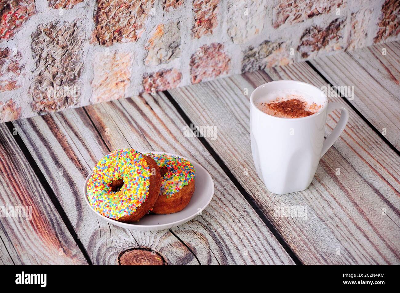 A plate with two fresh donuts in multi-colored sprinkles and a mug of ...