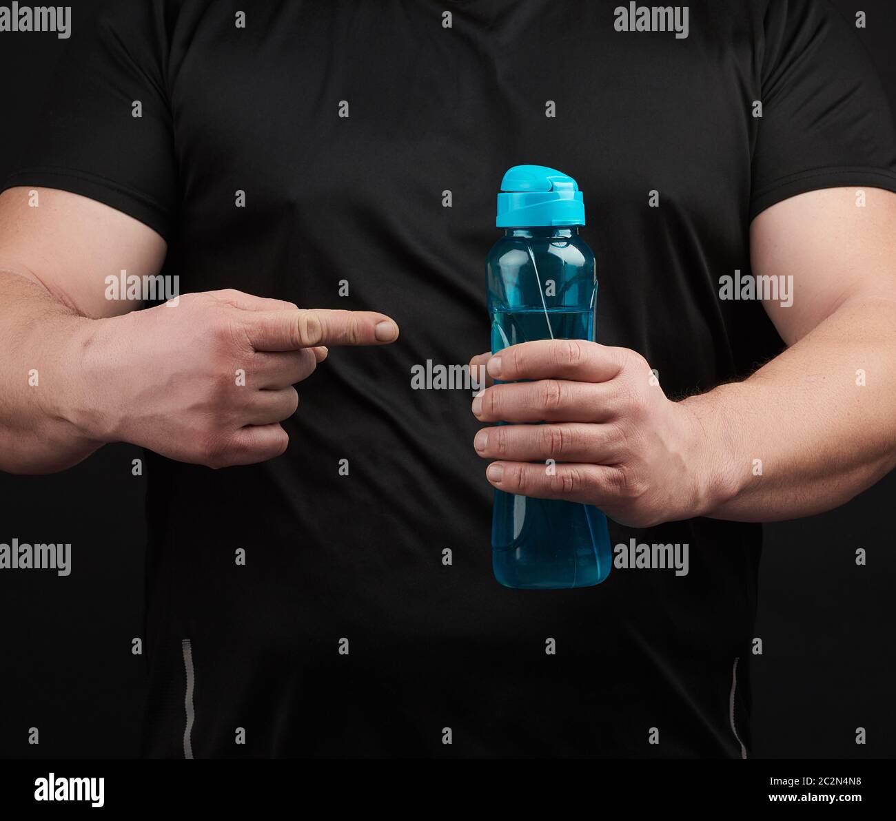 adult male athlete with muscles holds a plastic bottle of water ...