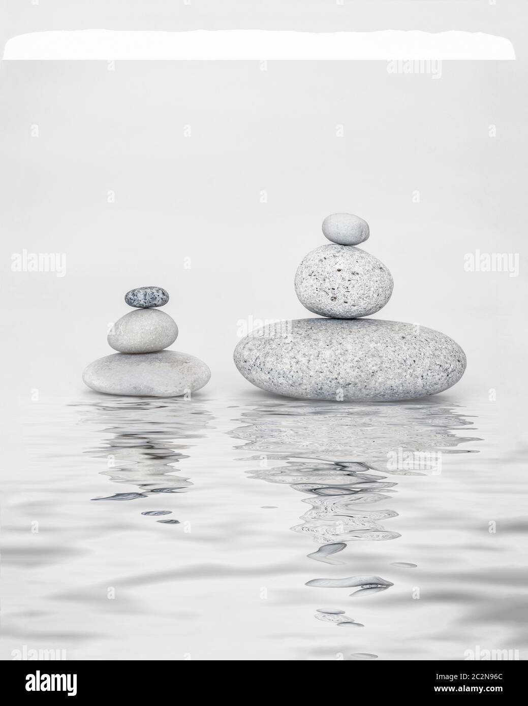 Two balanced pebble stone cairns reflecting in water across a white ...