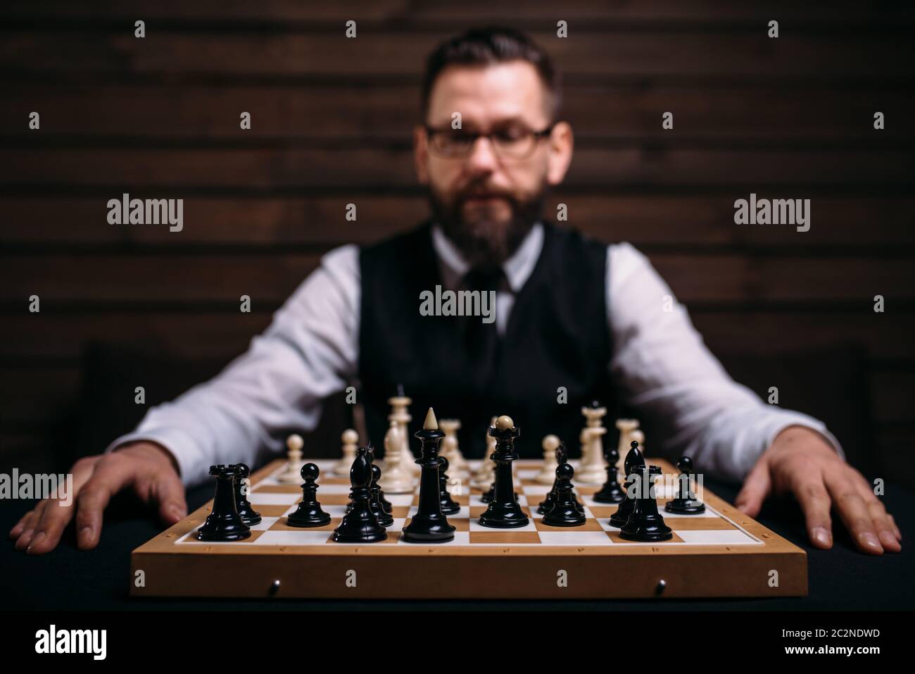Male player in glasses sitting against the chess board with the pieces ...