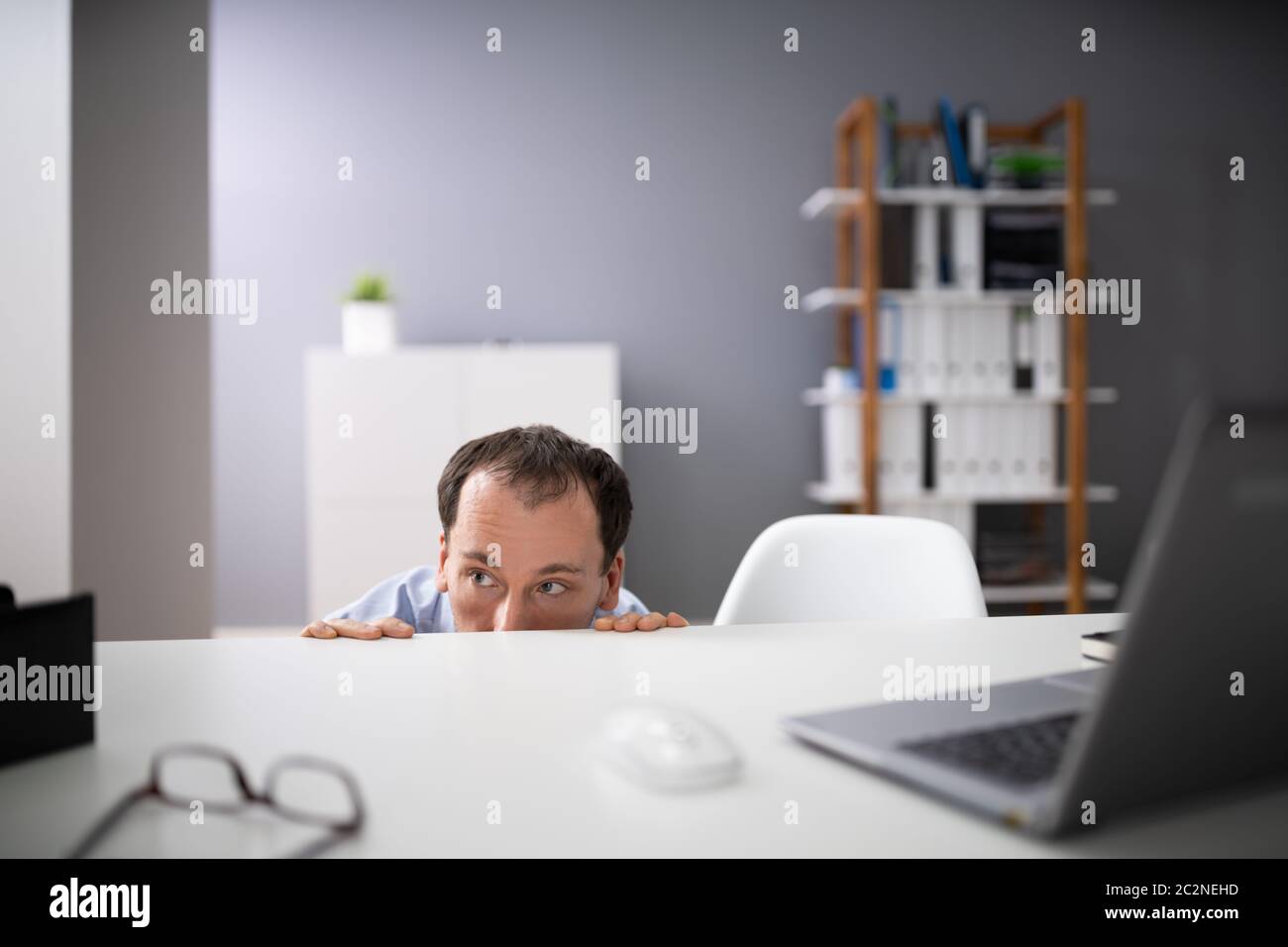 Frightened Young Businessman Hiding Behind Chair At Workplace Stock ...