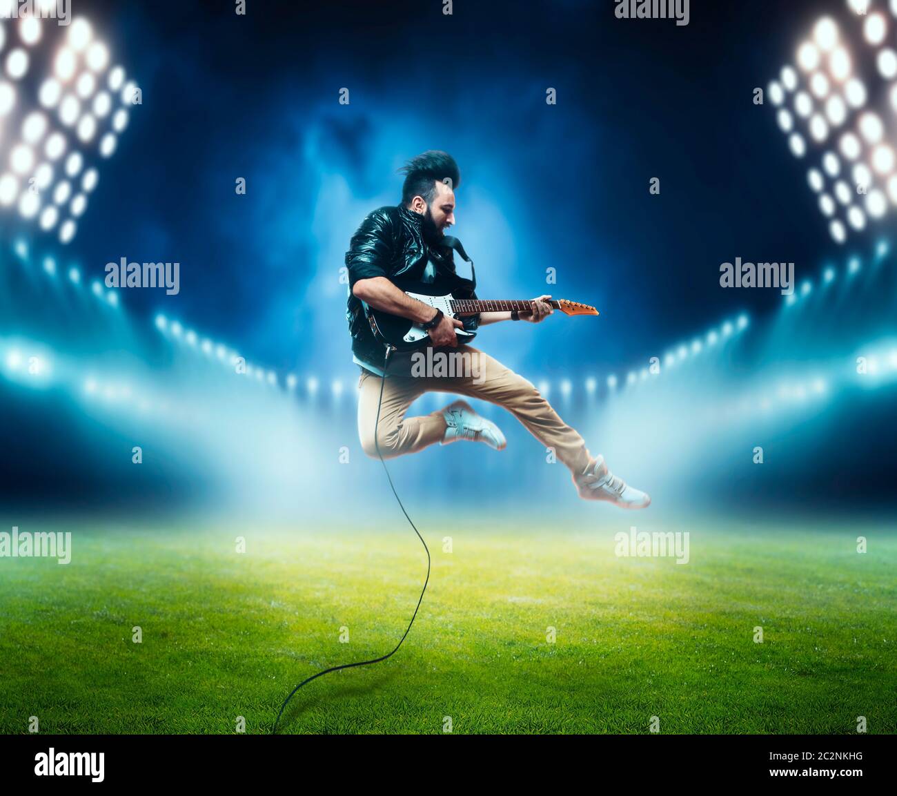Male performer with electro guitar in a jump on the stadium stage with ...
