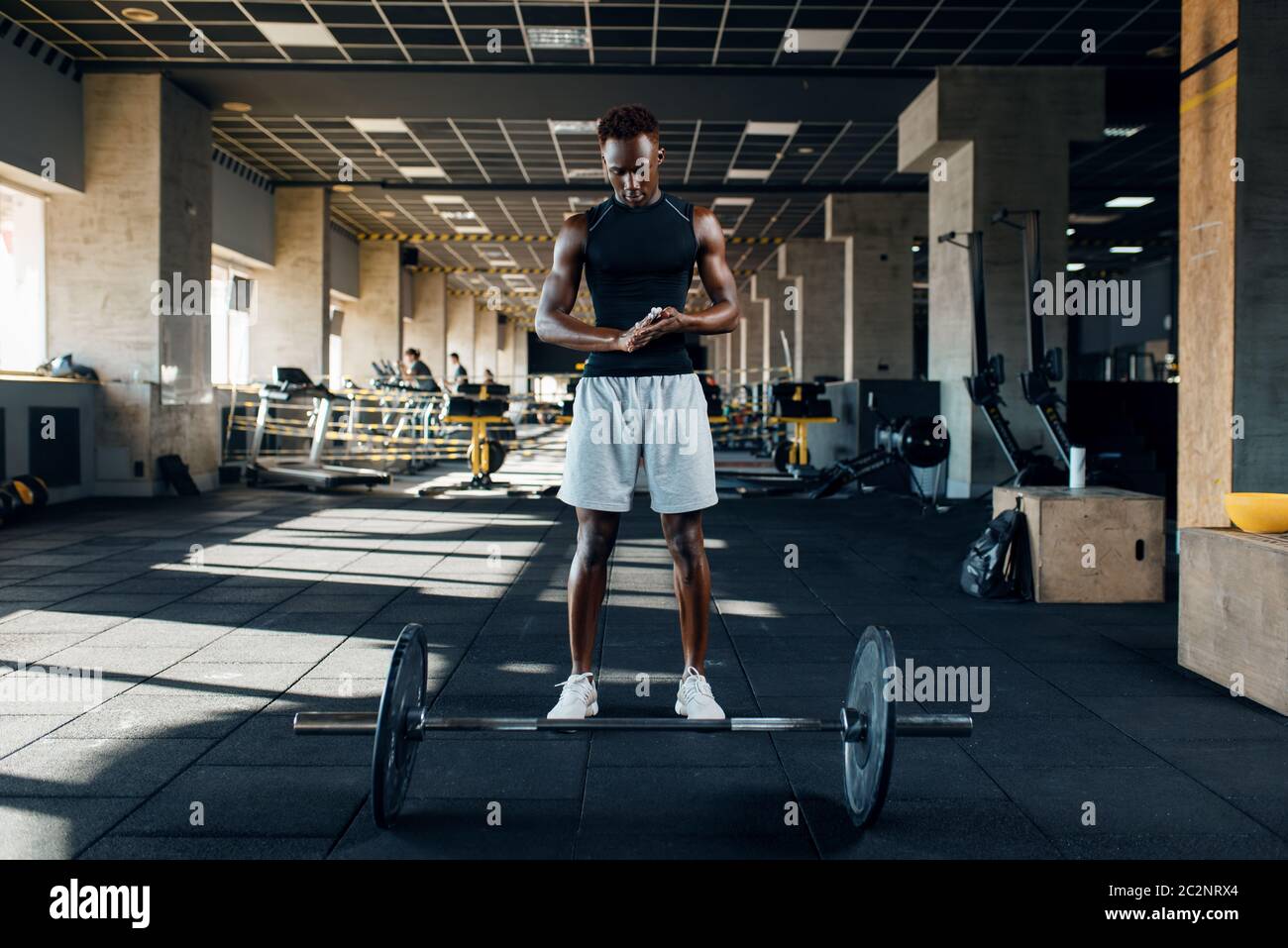 Muscular athlete in sportswear prepares for exercise with barbell on ...