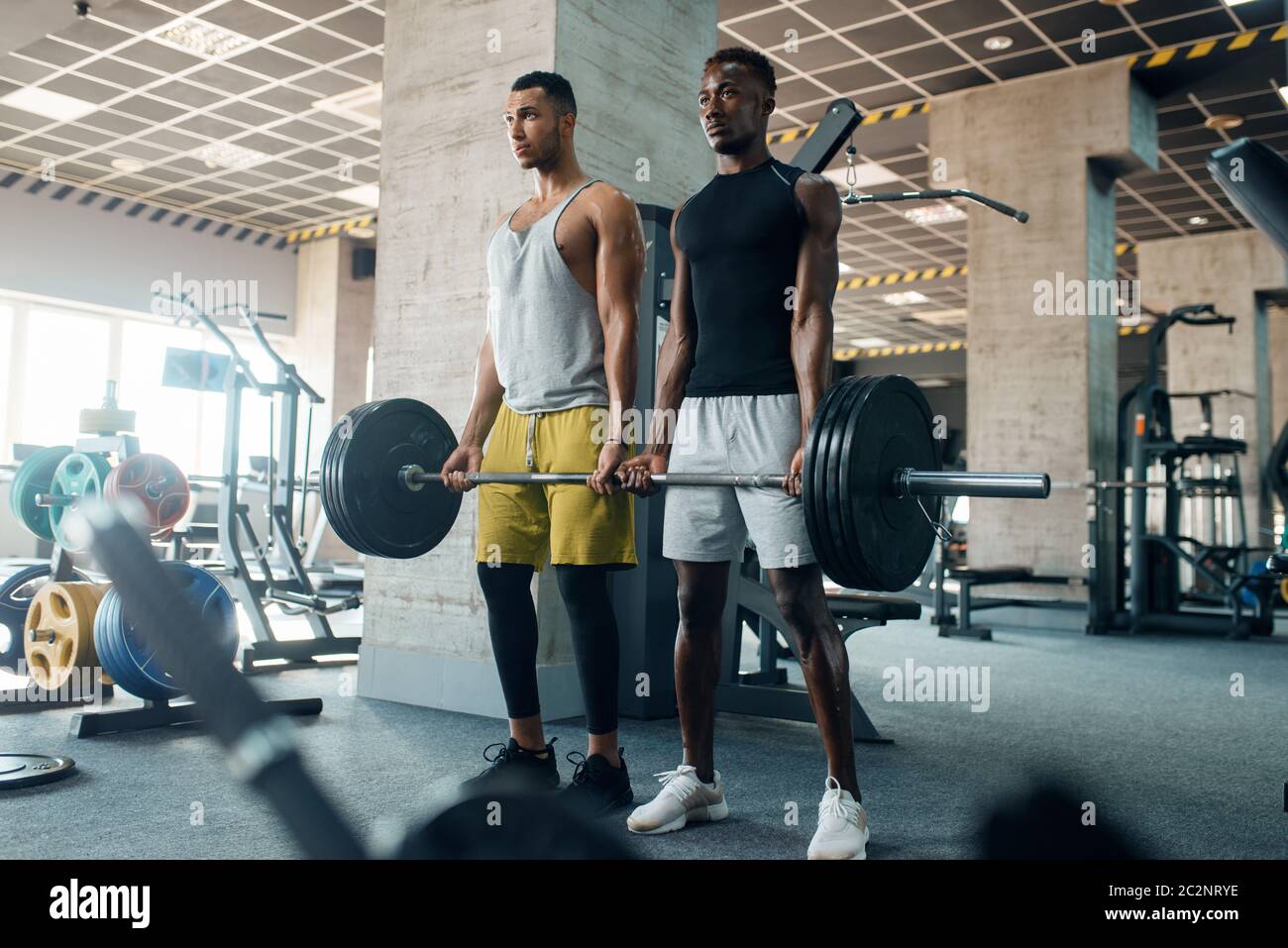 Two muscular men poses with heavy barbell on training in gym. Workout ...