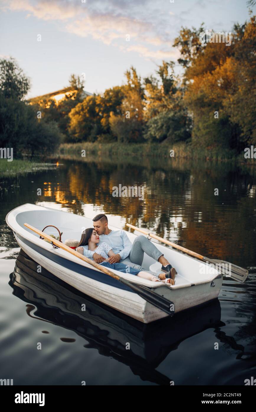 Love couple lying in a boat on quiet lake at summer day at sunset ...