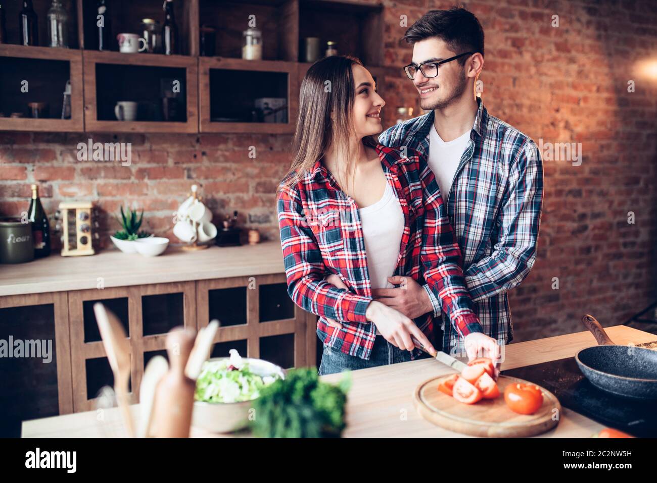 Husband hugs wife while she cooking fresh vegetable salad in bowl on ...