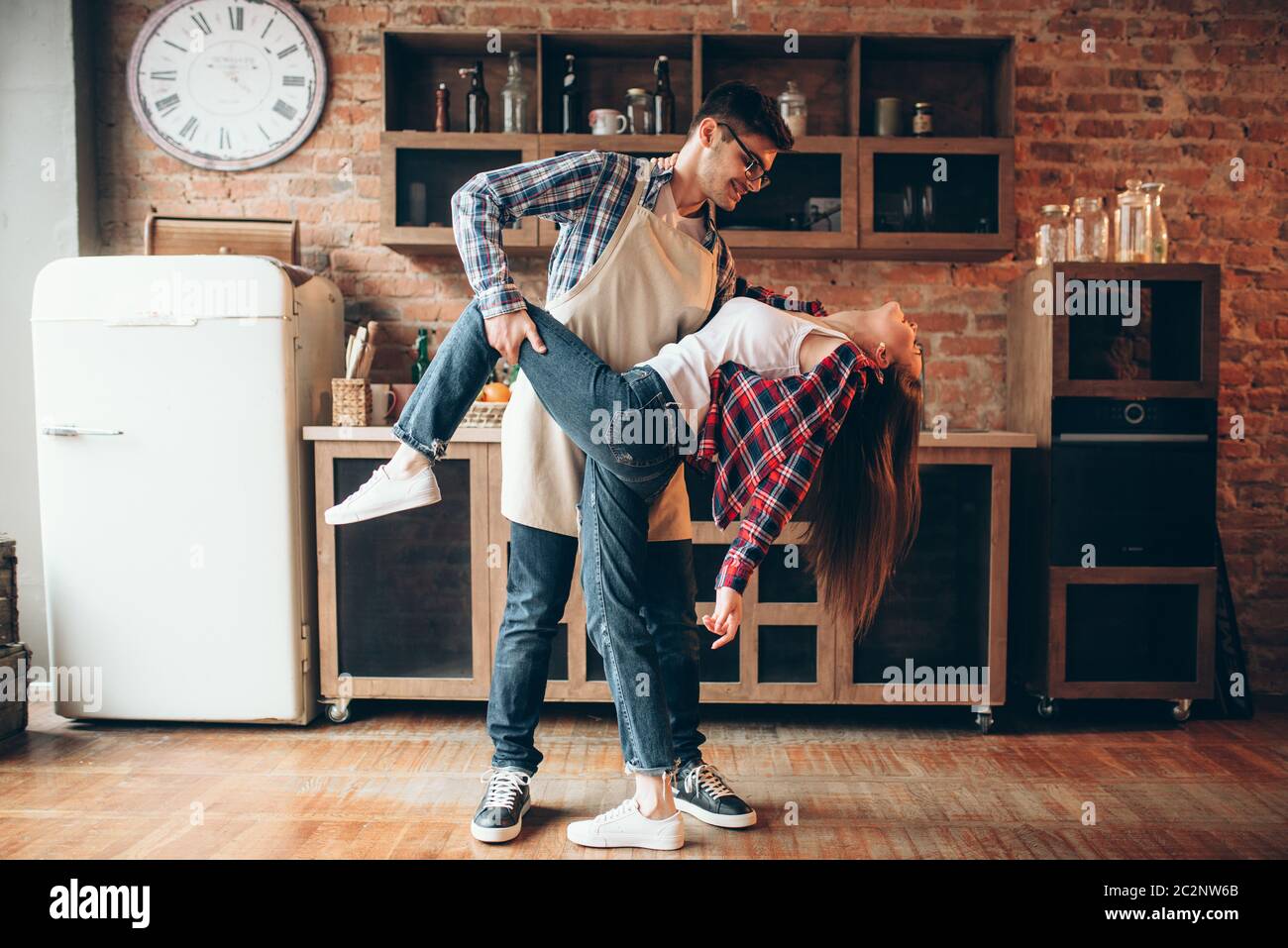 Playful love couple poses on the kitchen. Man in apron and young woman ...