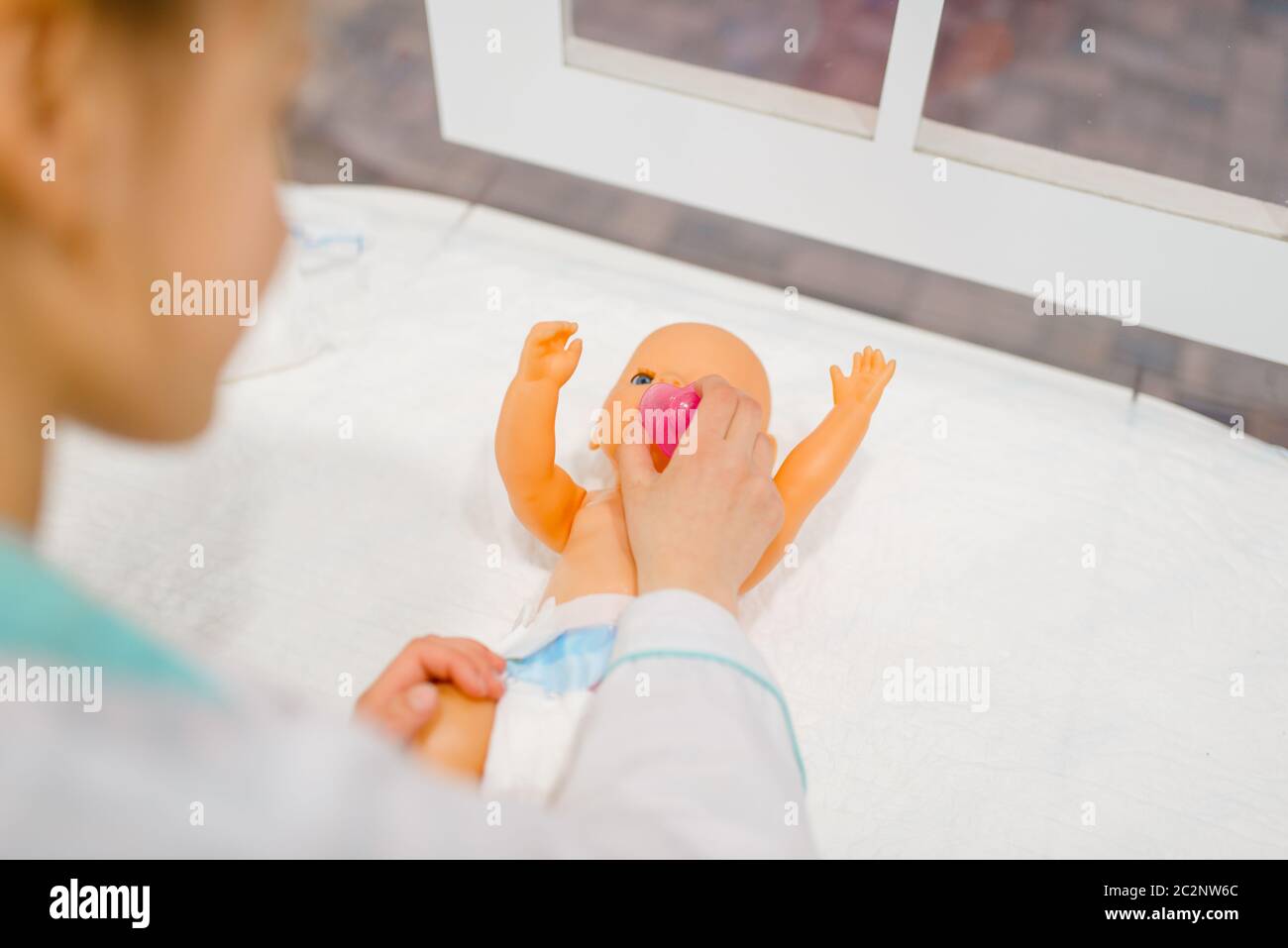 Little girl in uniform feeding toy doll, playing doctor, playroom. Kid ...