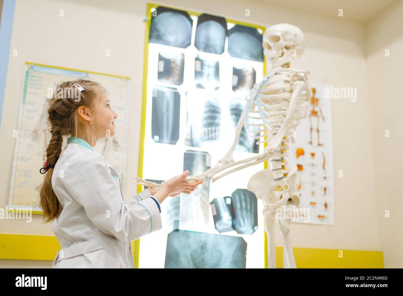 Little girl in uniform playing doctor with human skeleton, playroom ...