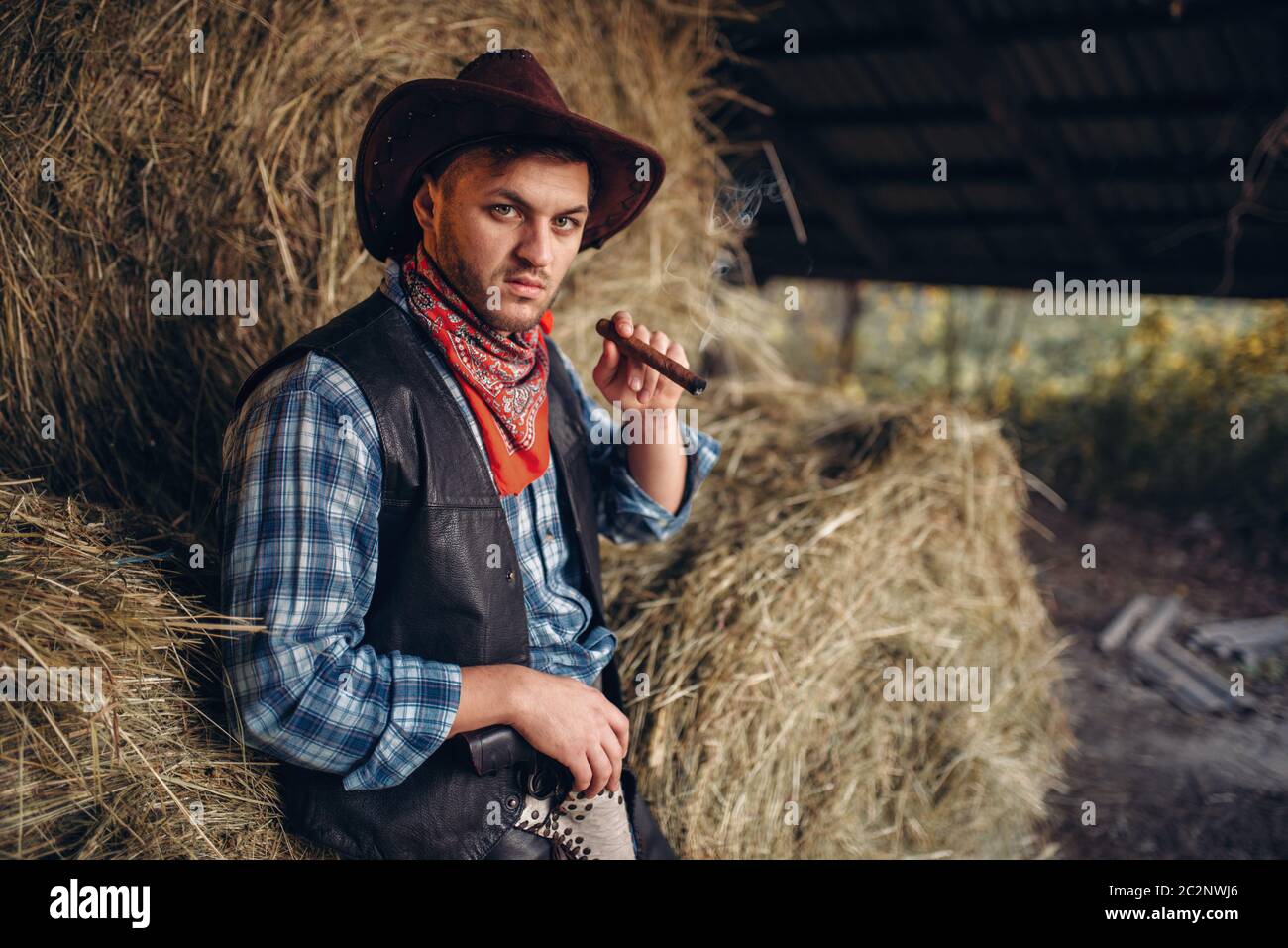 Brutal cowboy smokes a cigar, haystack on background, western. Vintage ...