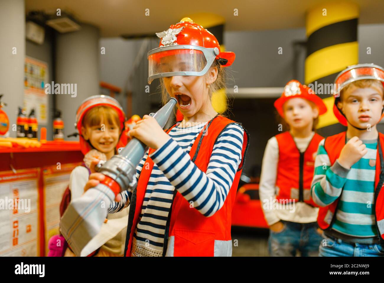 Female child in helmet and uniform having fun with hose in hands ...