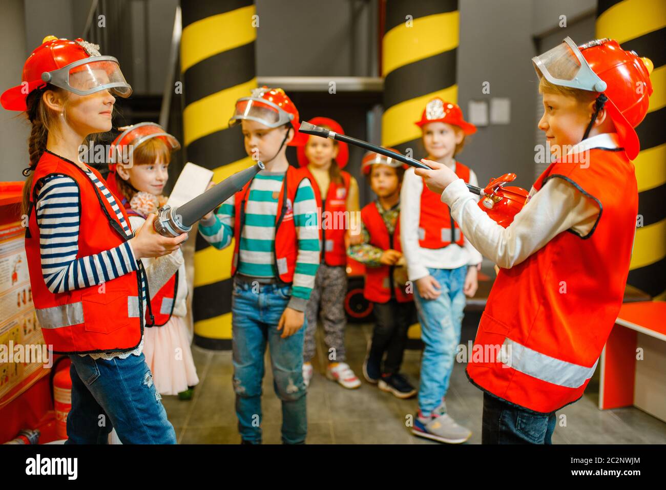 Children in helmet and uniform with hose and extinguisher in hands ...