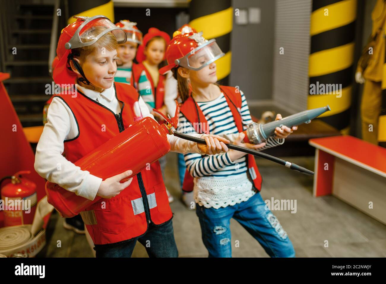 Children in helmet and uniform with hose and extinguisher in hands ...