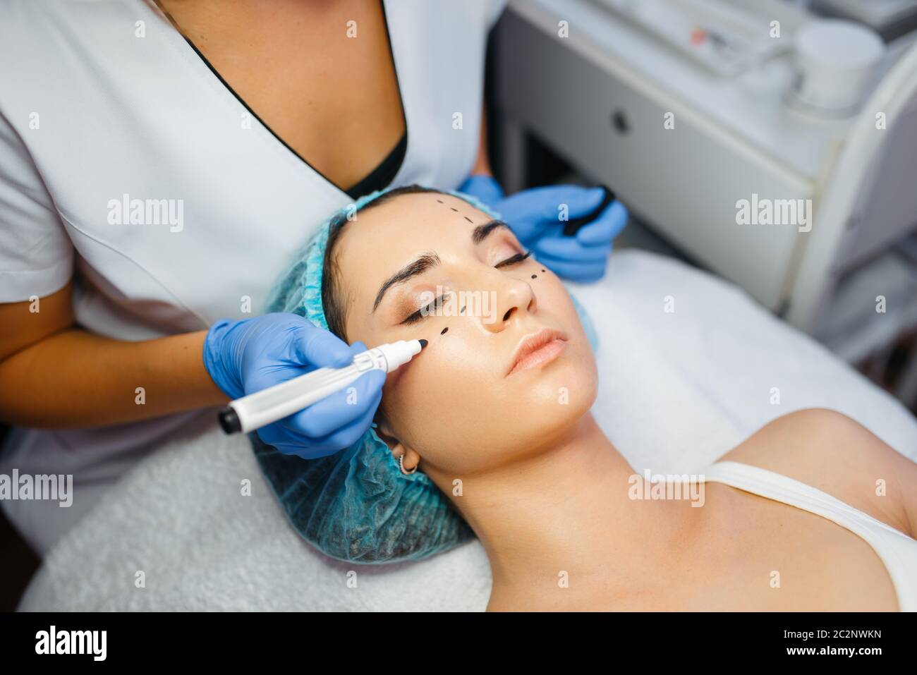 Cosmetician with marker puts dotted lines on female patient face, botox ...