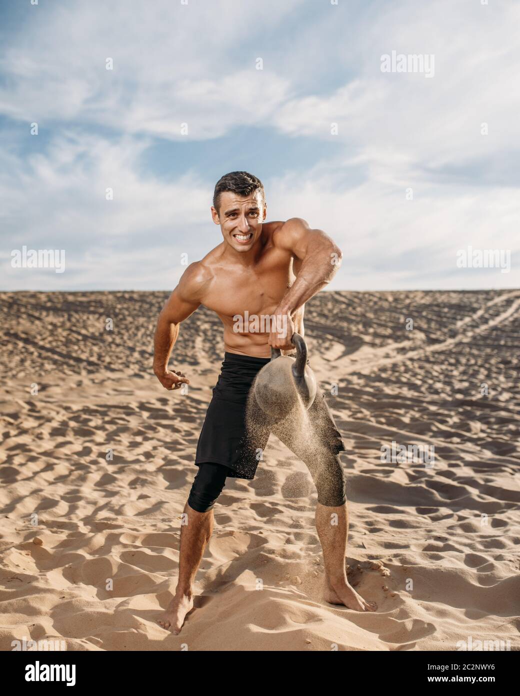 Male athlete doing exercises with kettlebell in desert at sunny day ...