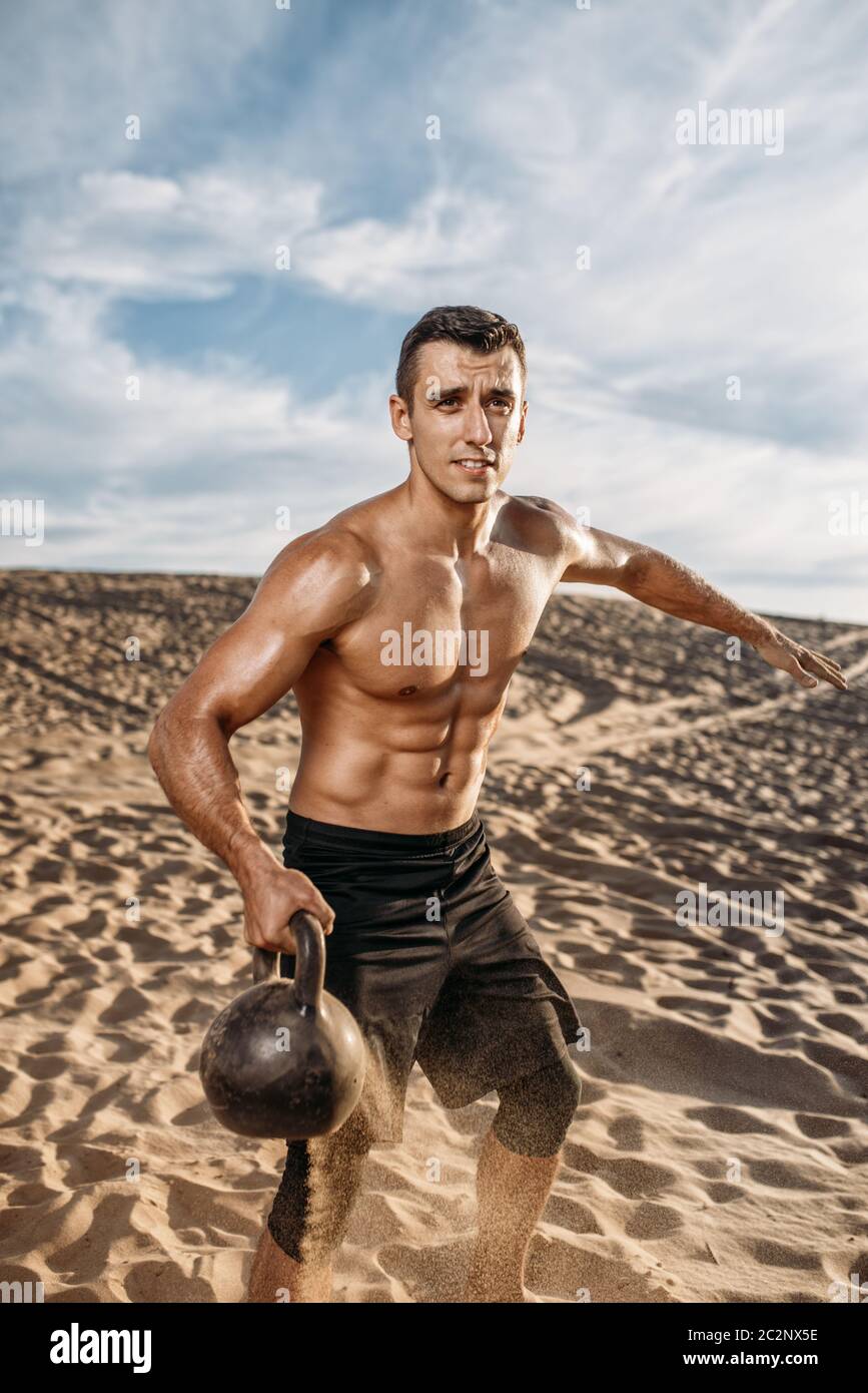 Male athlete doing exercises with kettlebell in desert at sunny day ...