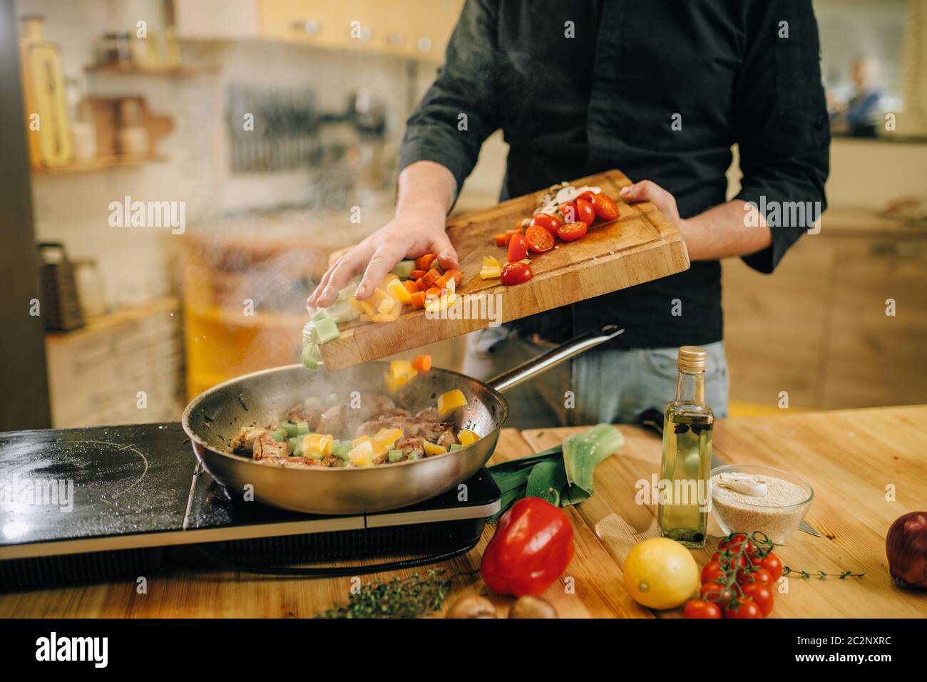 Male person puts vegetables into the frying pan with roasted meat on ...