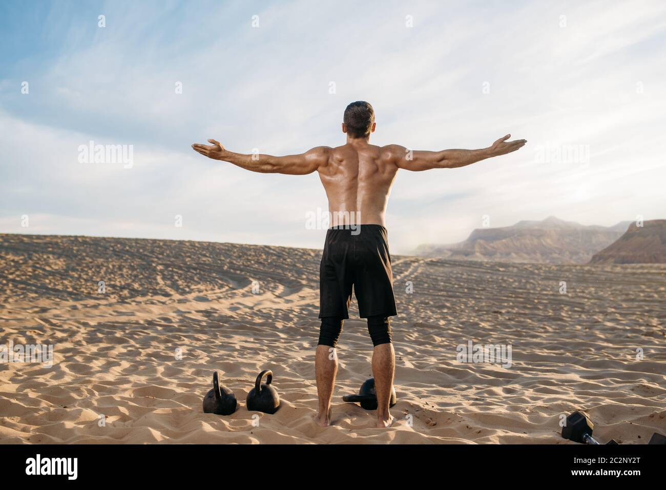Sportsman doing exercises with weights in desert at sunny day, back ...