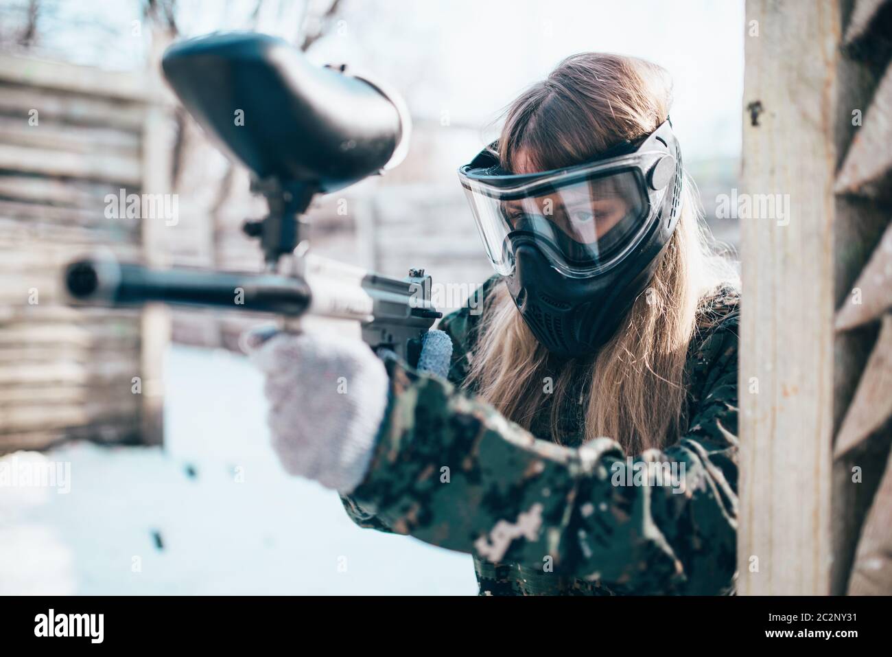 Female paintball player with marker gun in hands, winter forest battle ...