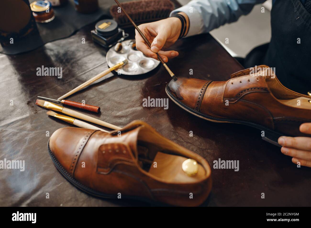 Bootmaker with brush tints shoes, footwear repair service. Craftsman ...