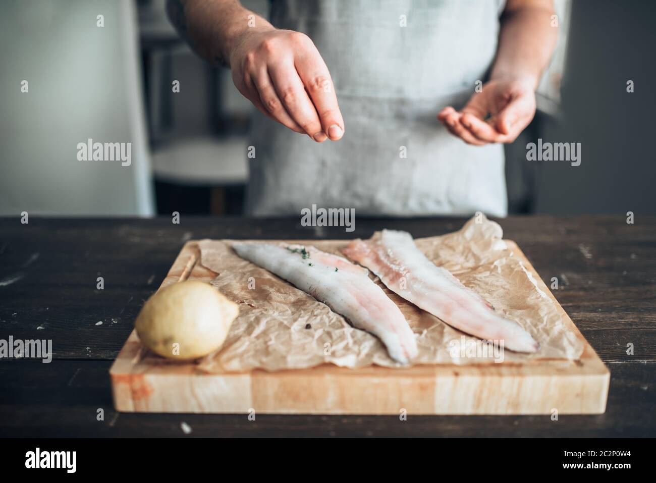 Male chef hands salting raw fish over wooden cutting board covered with ...