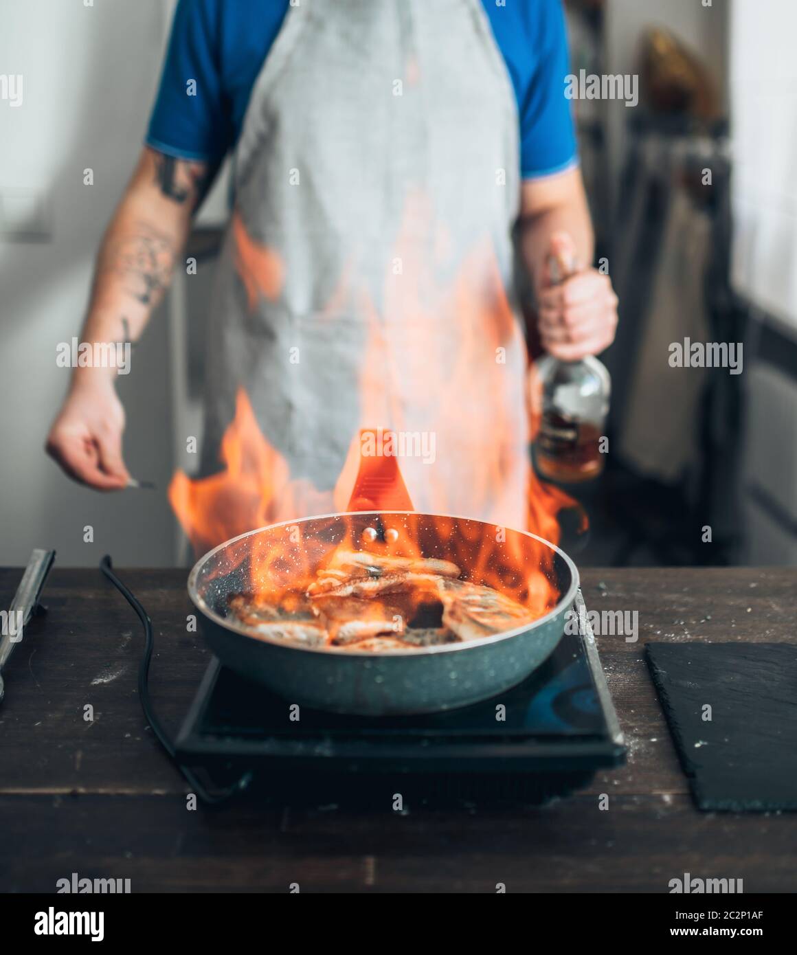 Male chef against frying pan with fire, cooking sea bass fish fillet ...