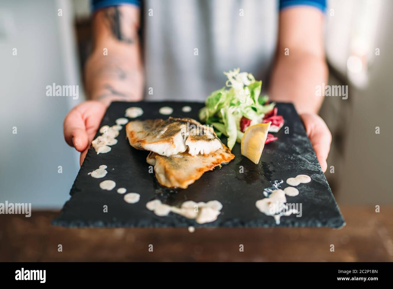 Male hands hold dish of fried fish fillet decorated with vegetables ...