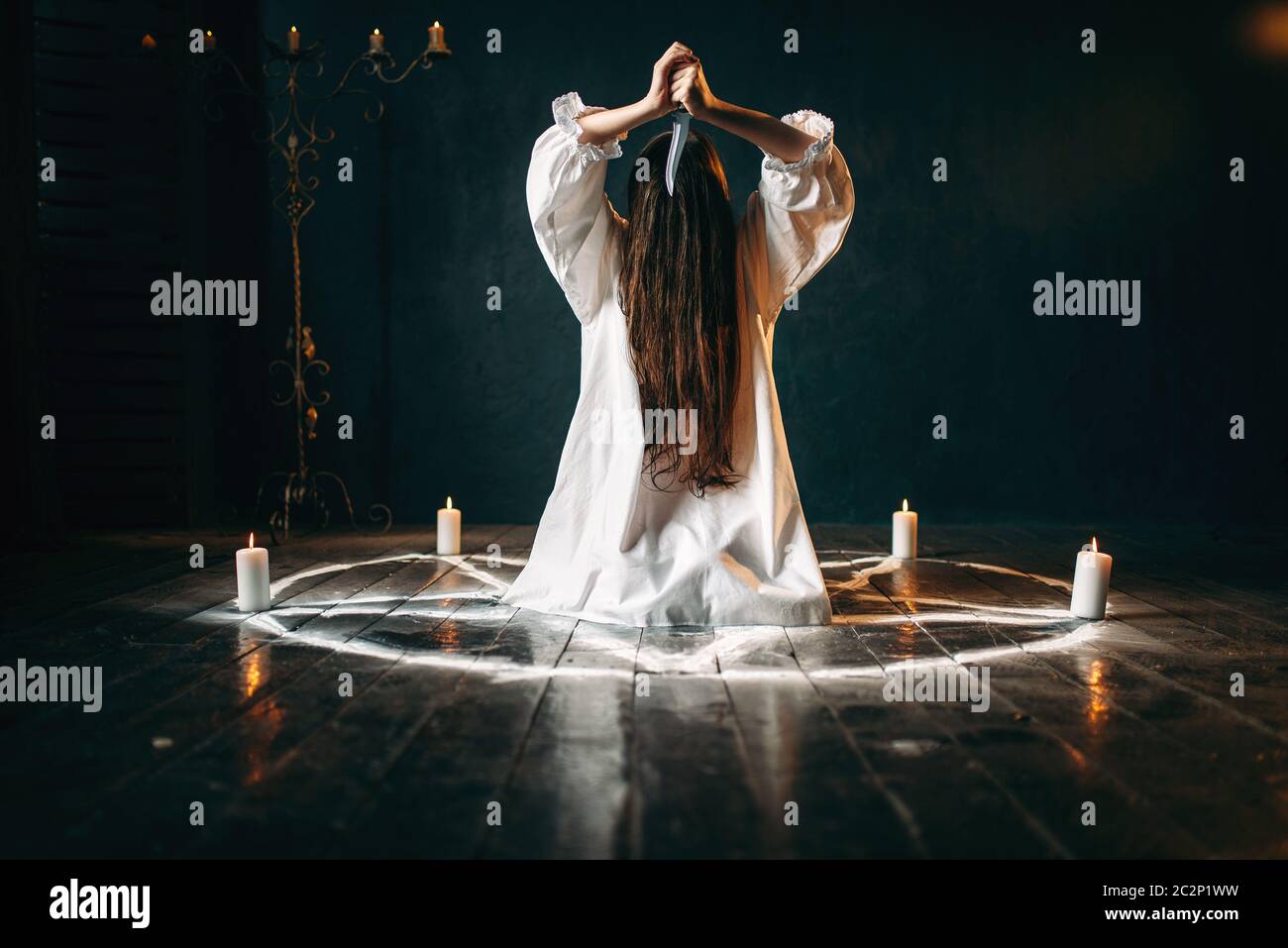 Woman with knife in hands sitting in pentagram circle with candles ...