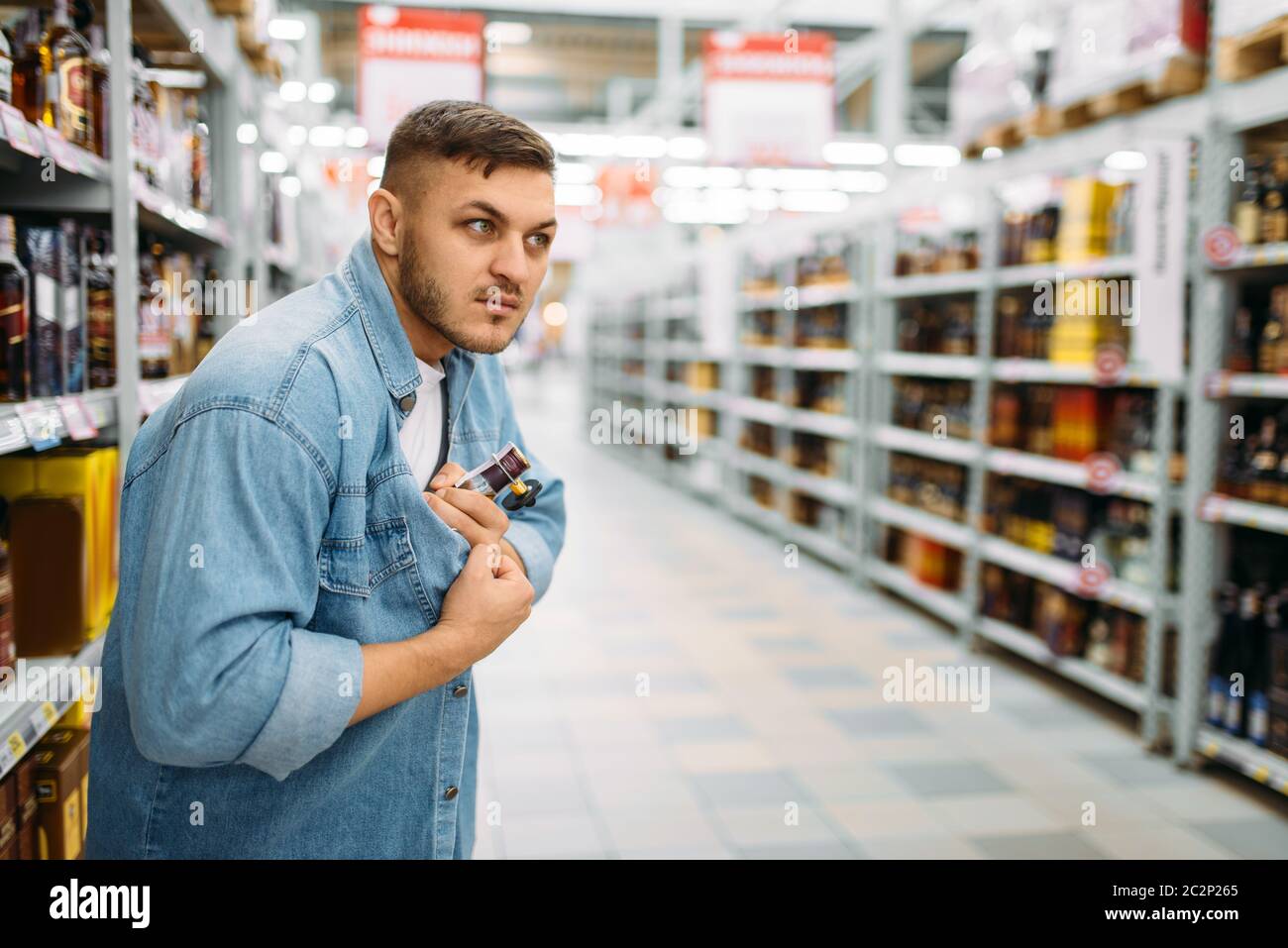 Man hides a bottle of alcohol under his shirt in supermarket. Male ...