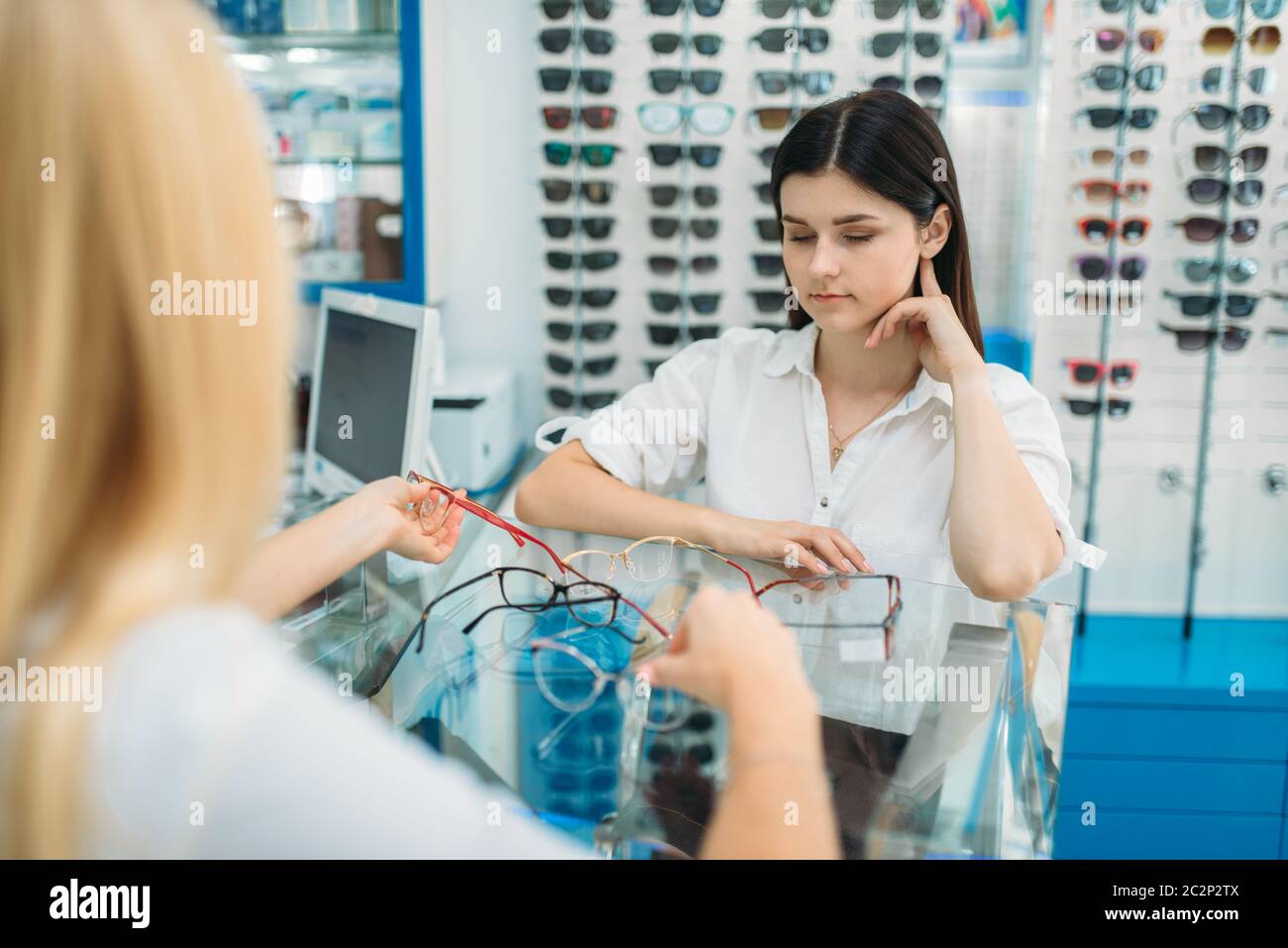 Female optician and woman chooses glasses frame in optics store ...